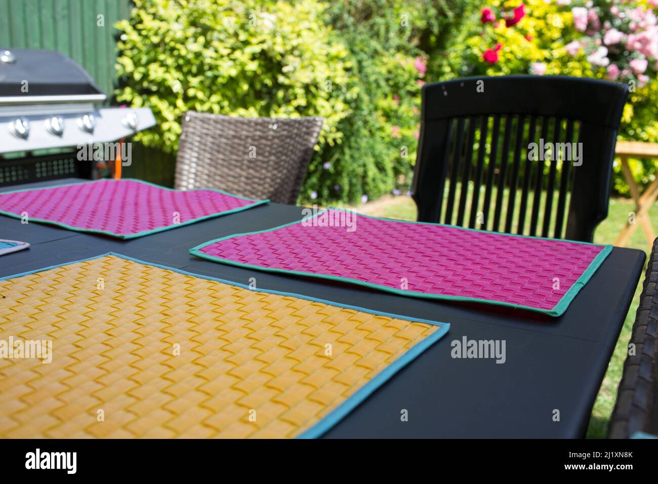 A green plastic table and chairs laid out with place mats in a garden ...