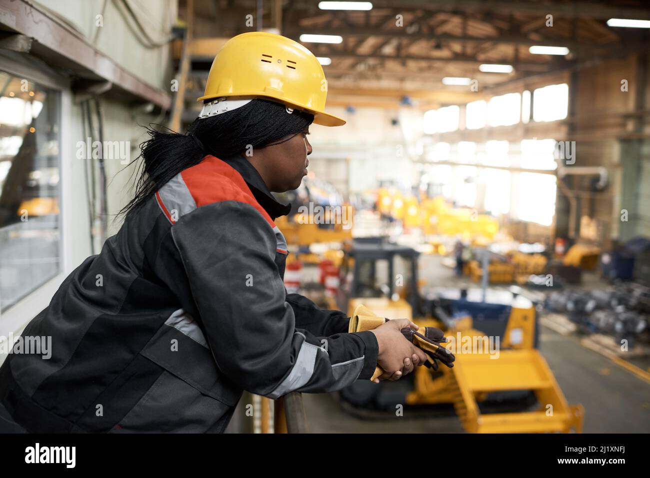 African female worker in uniform and hardhat standing on balcony and ...