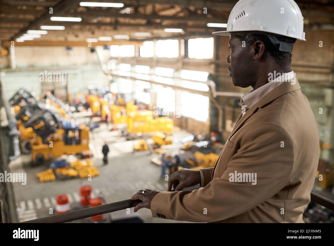Serious African engineer in work helmet standing on balcony and ...