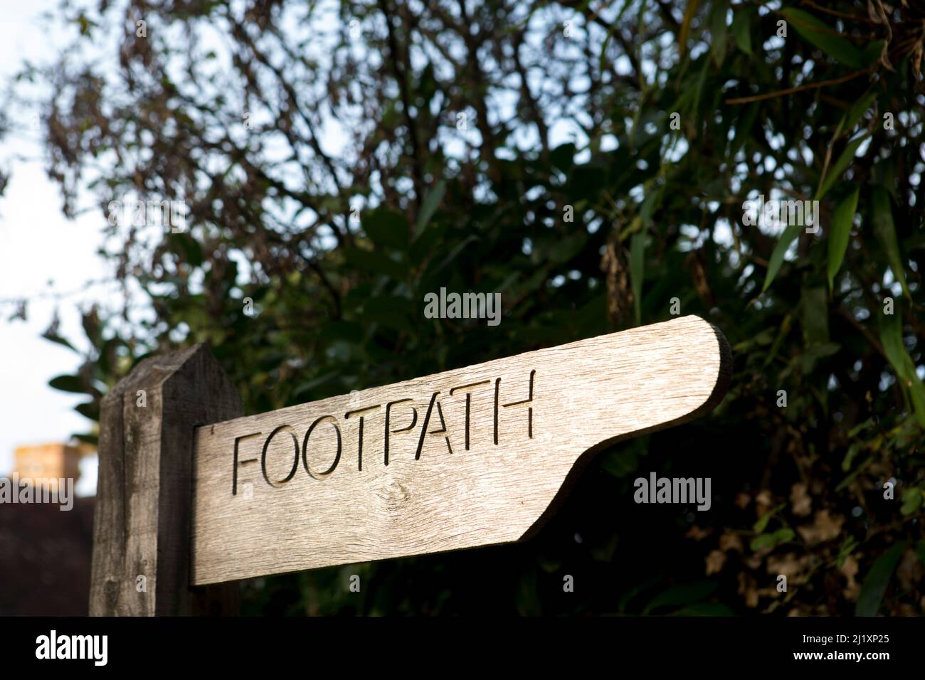 A wooden post in the countryside with a footpath sign pointing the ...