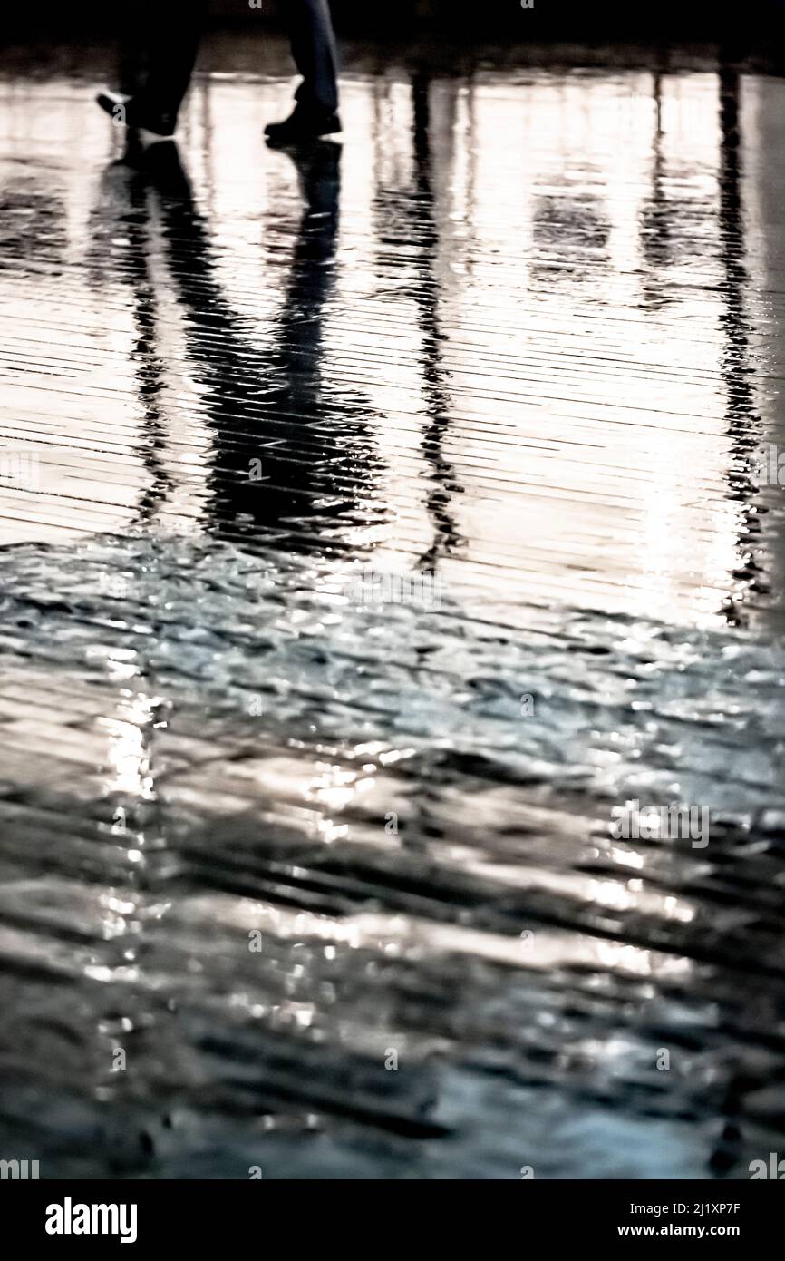 People walk along a rain soaked street made of tiles reflected in the ...