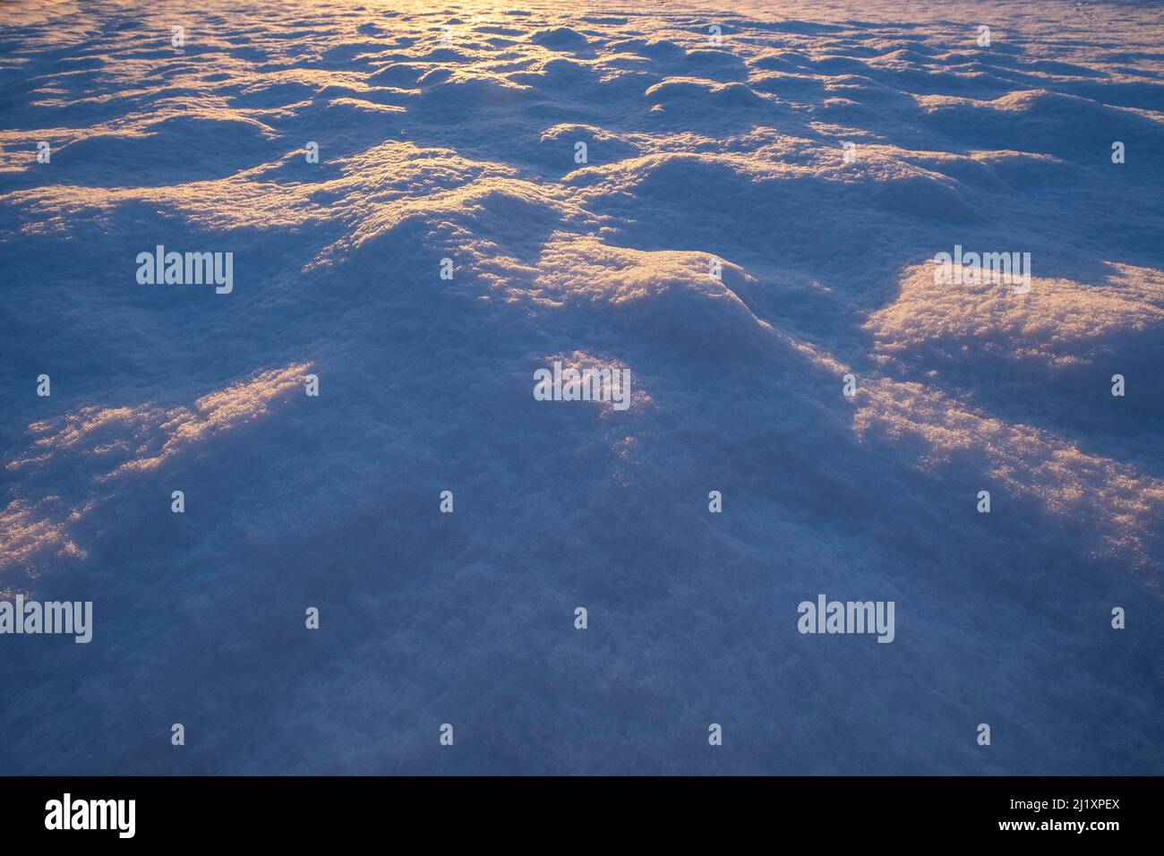 The sun sets over a field covered in snow highlighting the undulating ...