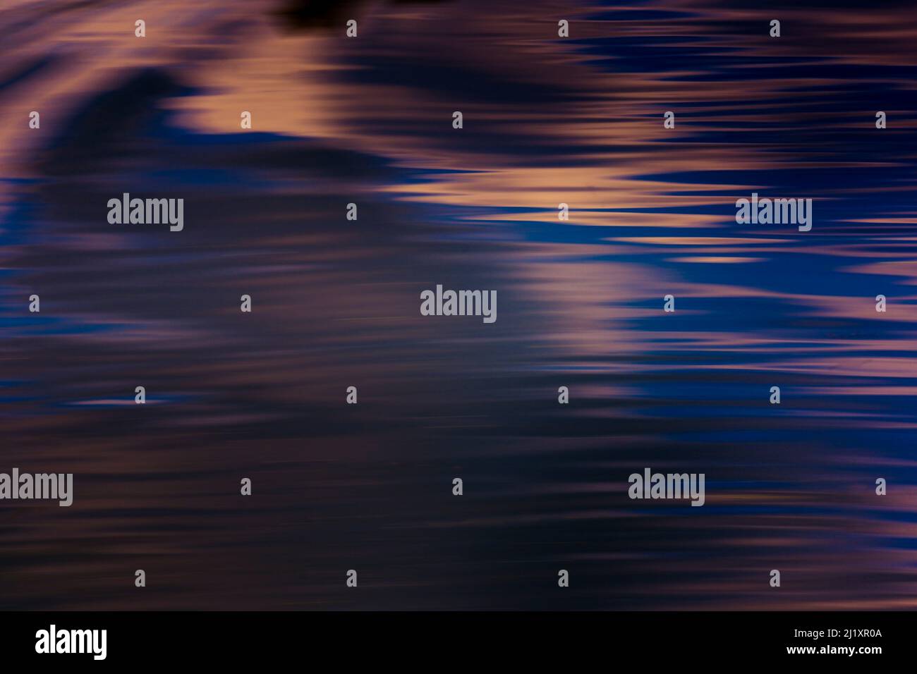 Small waves and ripples reflecting the colourful sky on the surface of ...