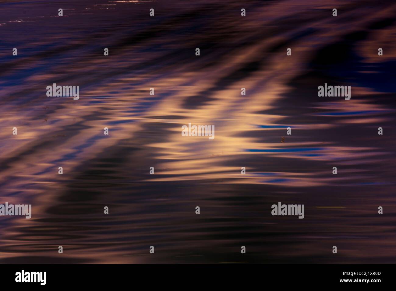 Small waves and ripples reflecting the colourful sky on the surface of ...