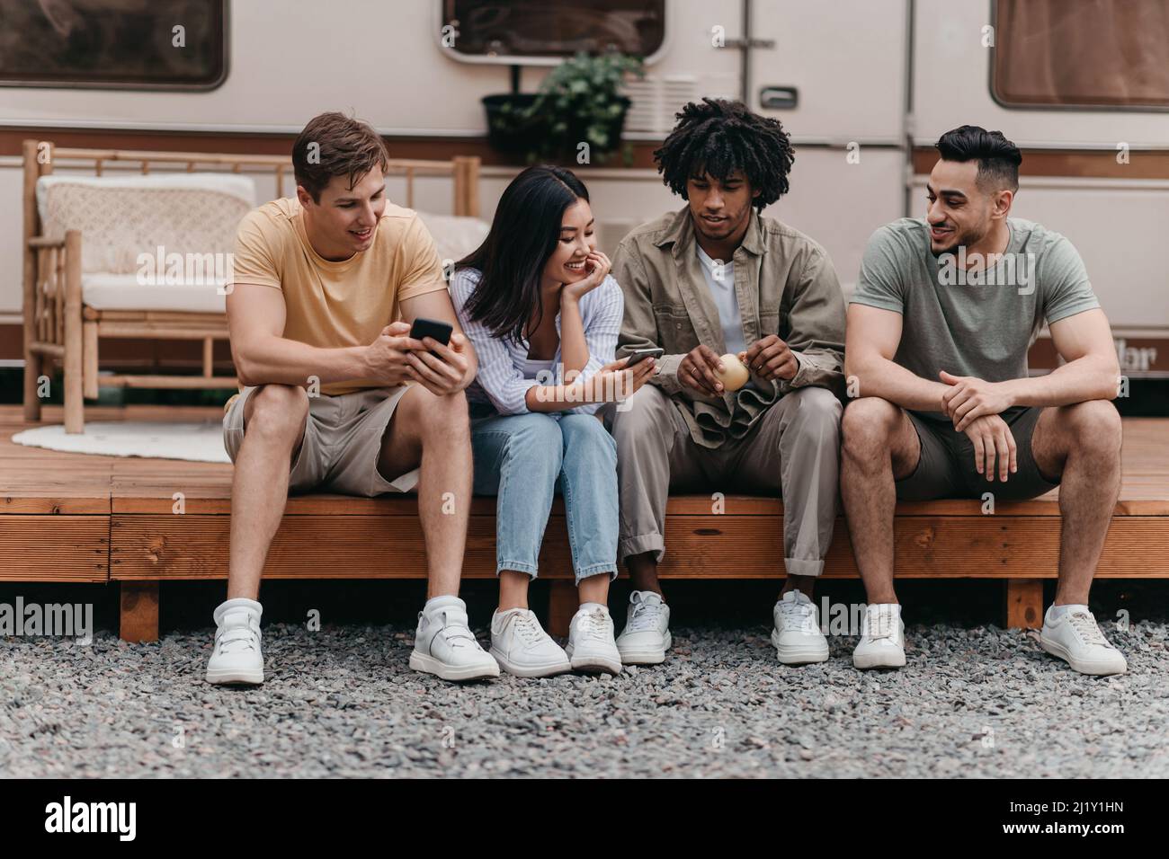 Group of diverse friends sitting near camper van, speaking to each ...