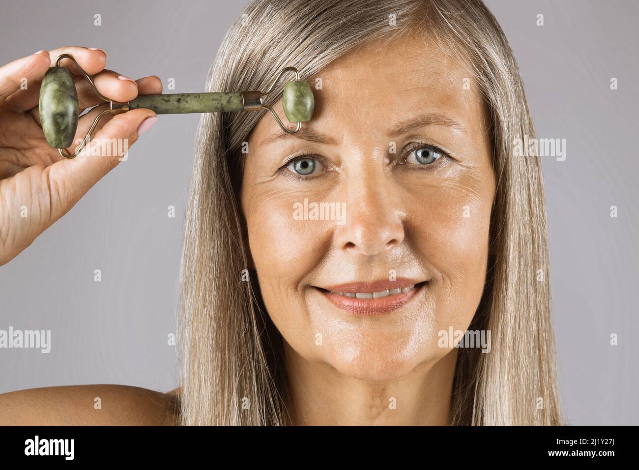 Happy beautiful woman with grey hair and wrinkles massaging face skin ...