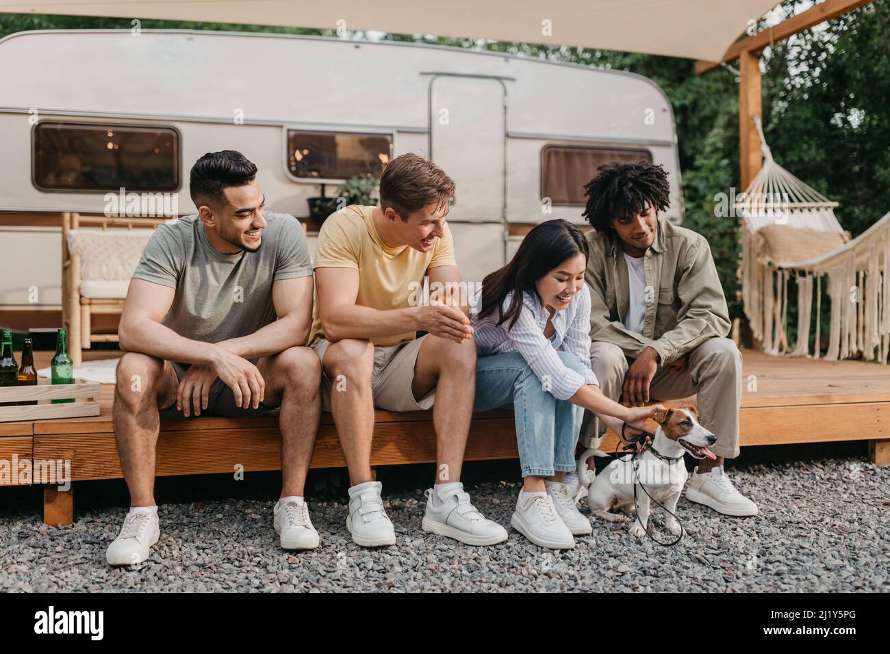 Group of diverse young friends sitting near camper van with pet dog ...