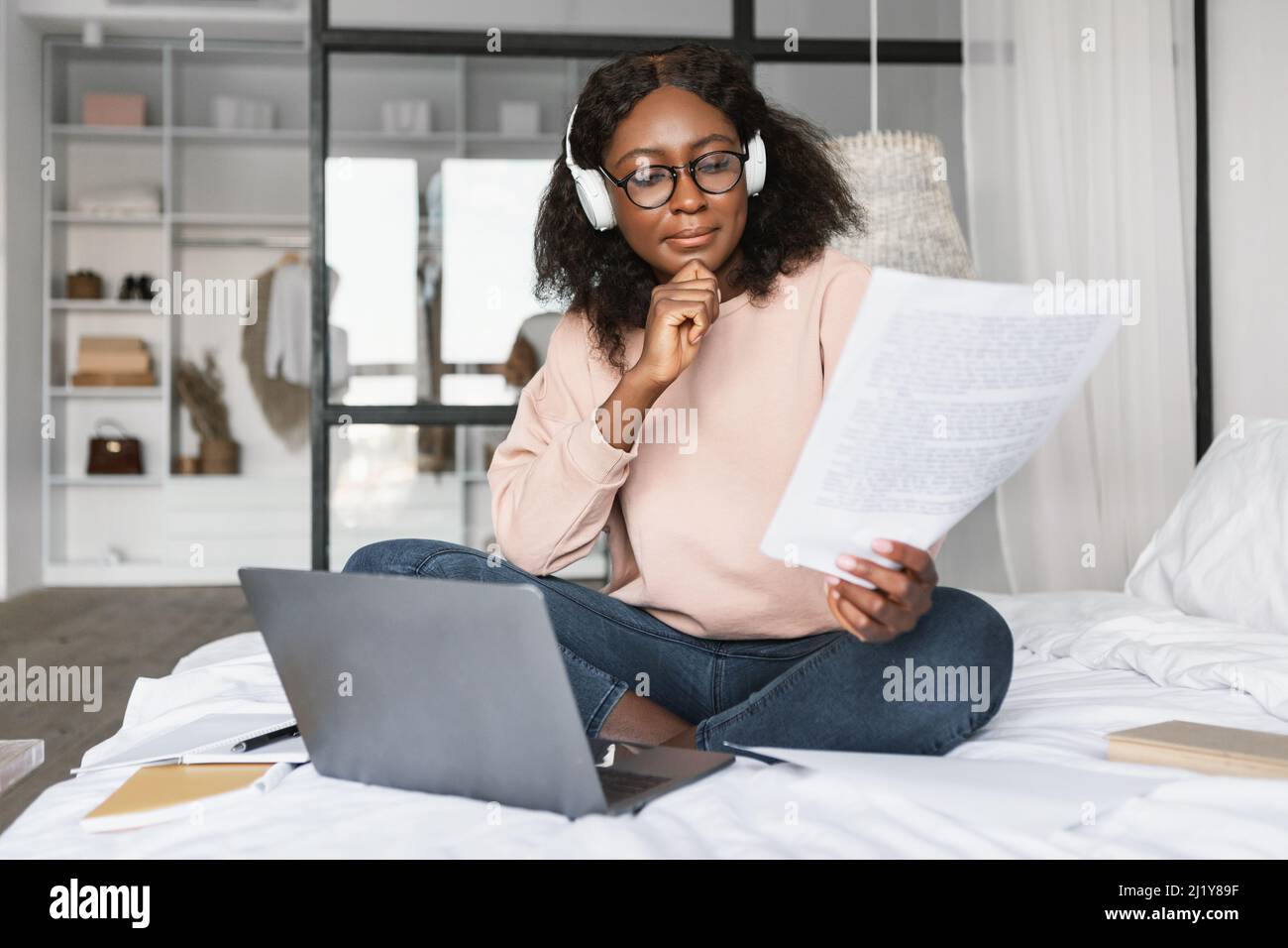 African Lady Reading Paper Using Laptop Computer Wearing Headphones ...