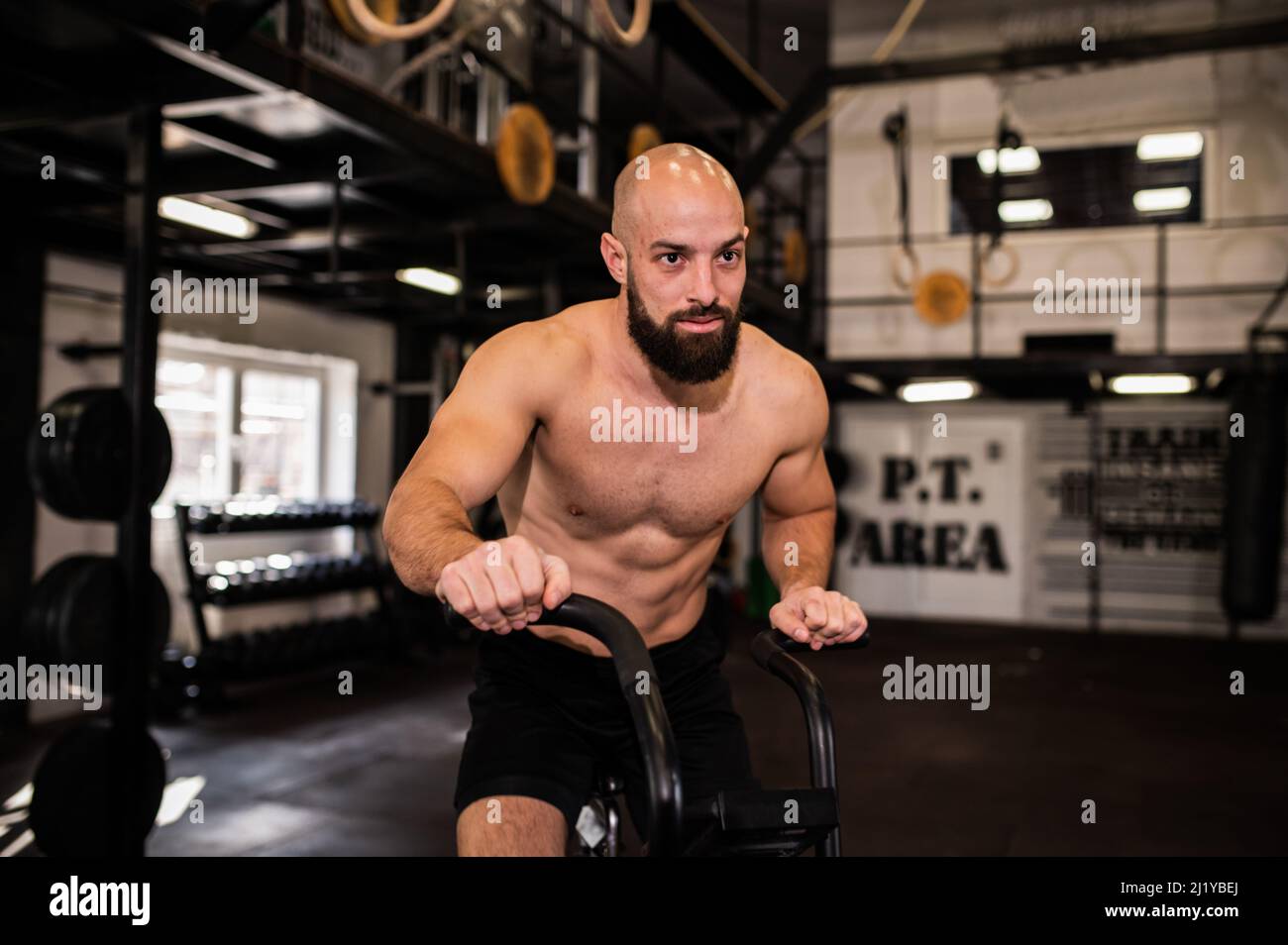 An attractive young muscular man exercises hard on a bicycle in his ...