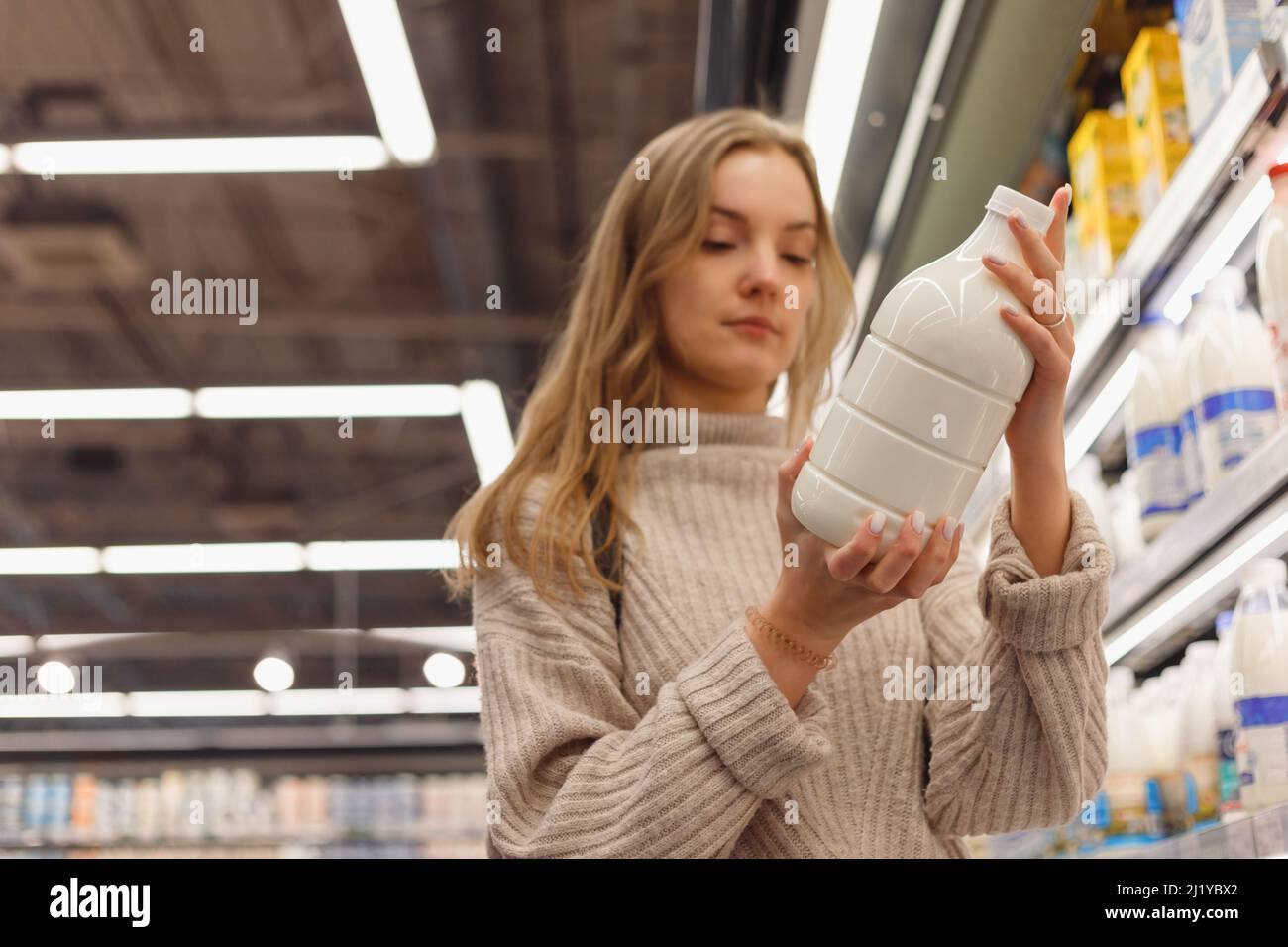 Grocery Shopping. Female read milk bottle In shop standing near shelf ...