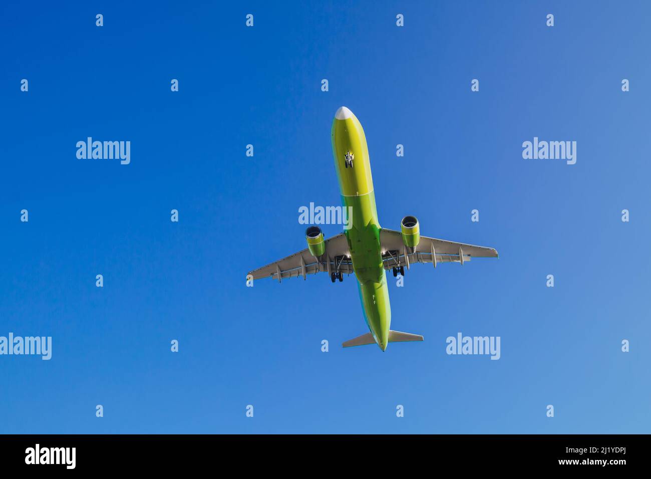 Passenger plane of yellow-green color flies in the blue sky with white ...