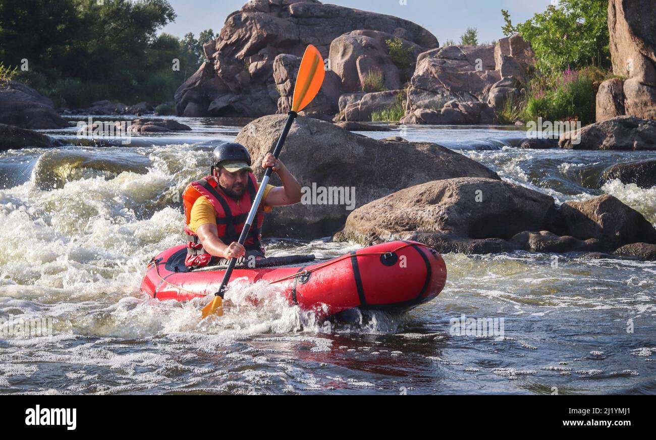 A man rowing inflatable packraft on whitewater of mountain river ...