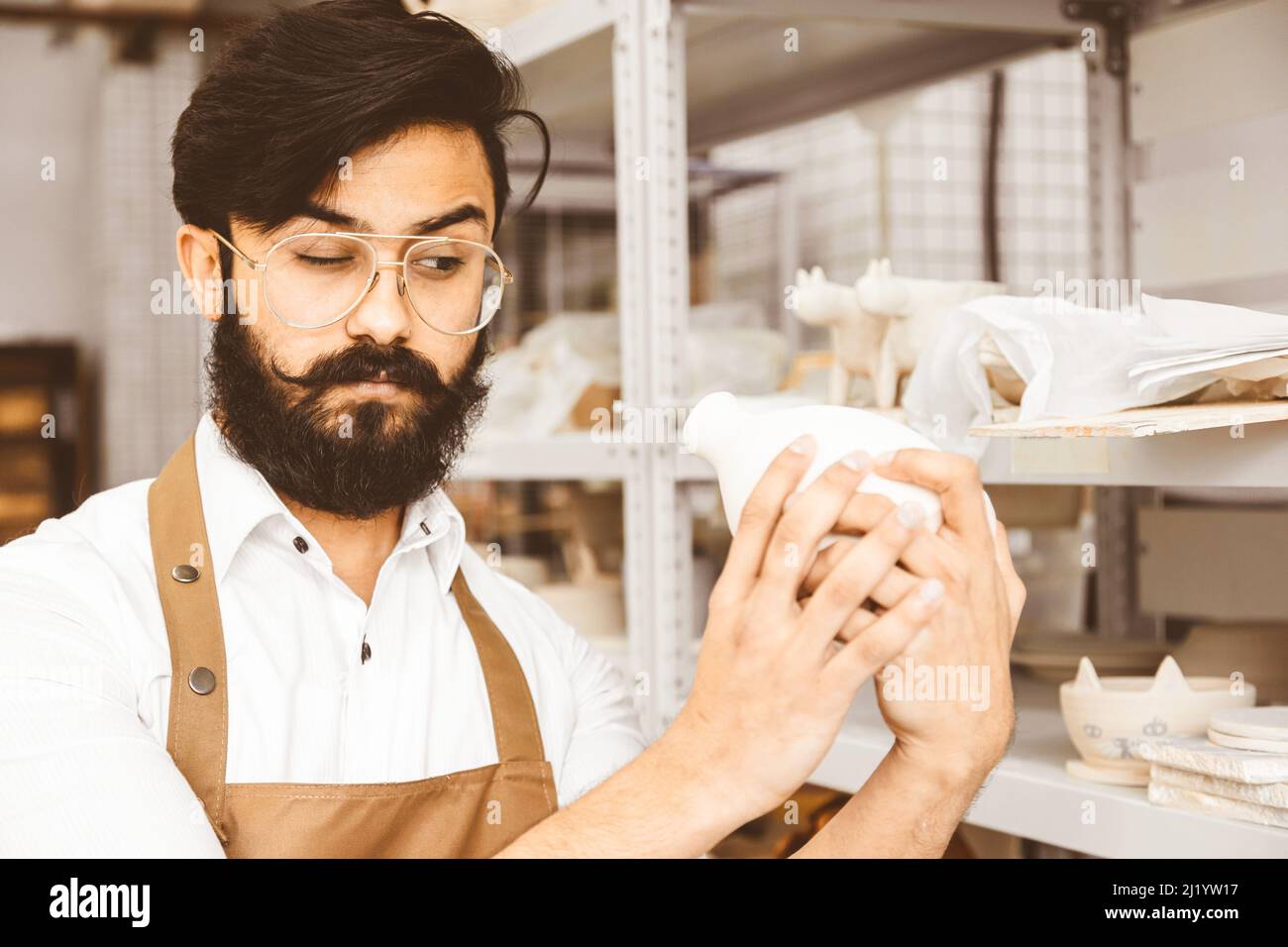 A young attractive male potter with a beard and mustache works in his ...