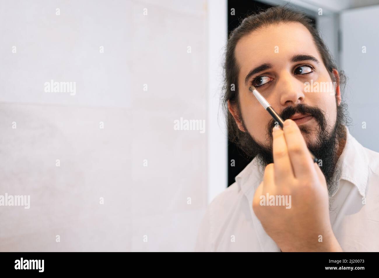 Young man applying make-up in front of the mirror. Daily make-up ...