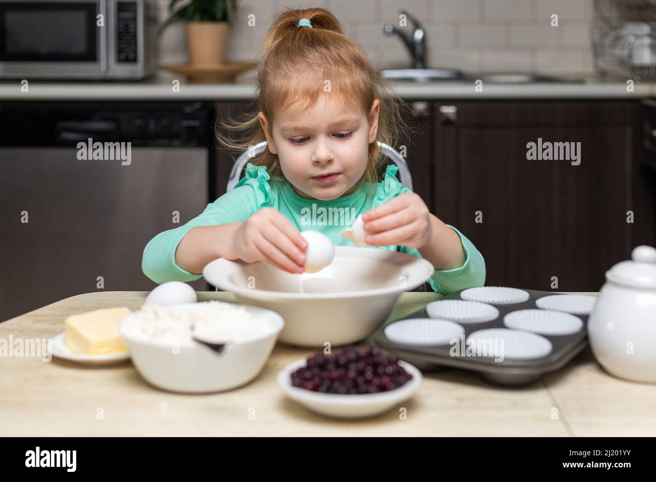 Little girl cooking in kitchen, breaking egg in bowl. Child sitting at ...