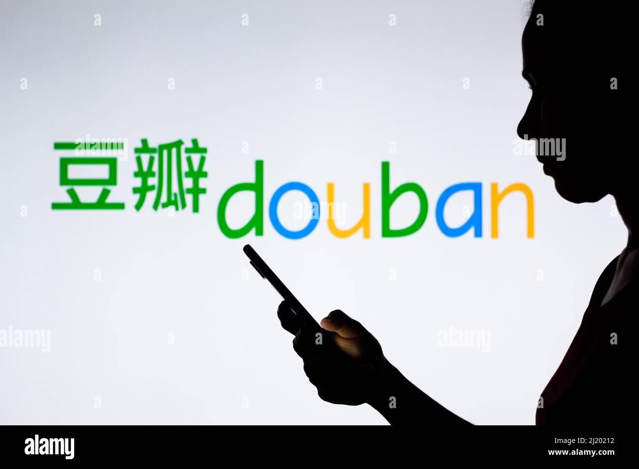 In this photo illustration, a woman's silhouette holds a smartphone with the Douban logo in the ...