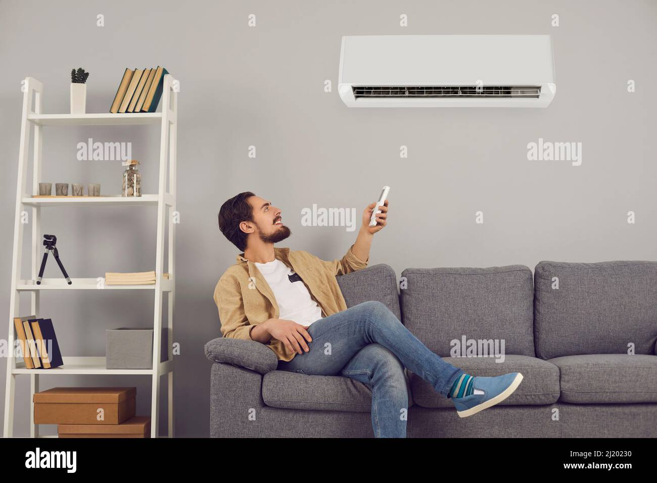 Happy man sitting on the sofa and setting a comfortable temperature on ...