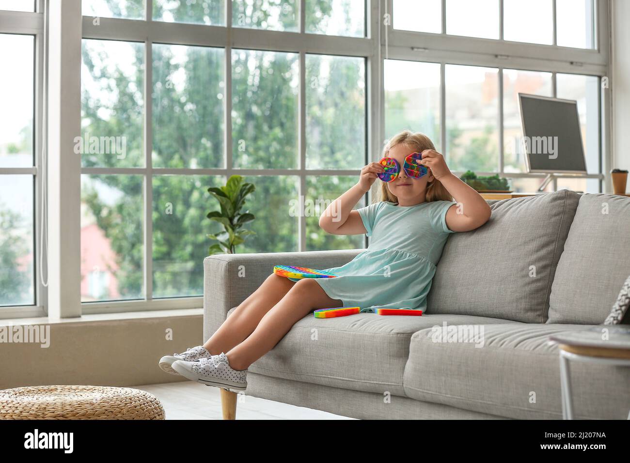 Little girl sitting on sofa with pop it fidget toys in room Stock Photo ...