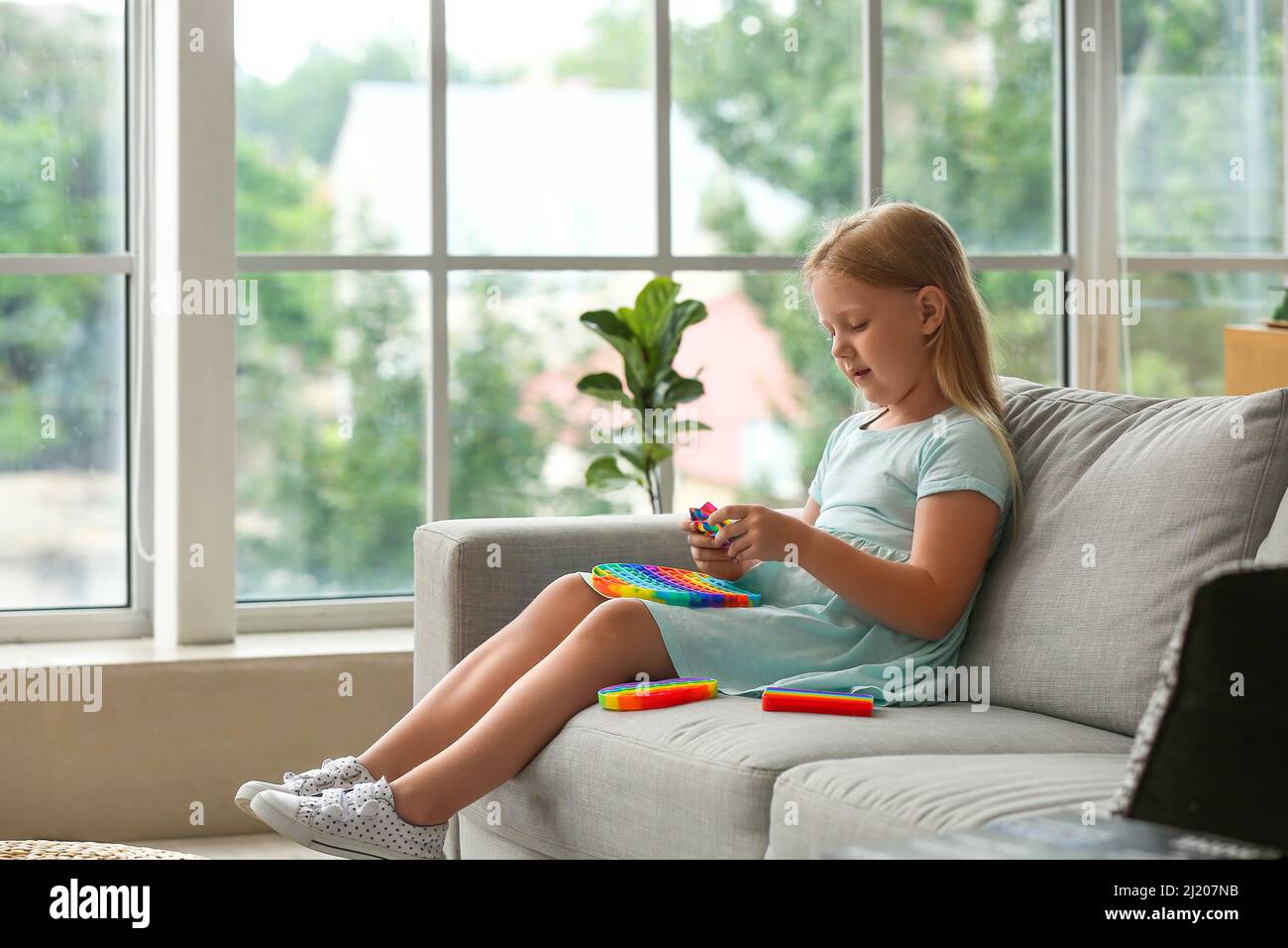 Little girl sitting on sofa and playing with pop it fidget toy in room ...