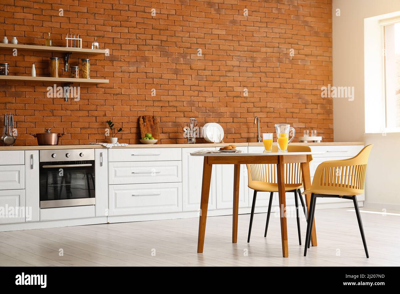 Interior of modern kitchen with dining table, white counters and brick ...