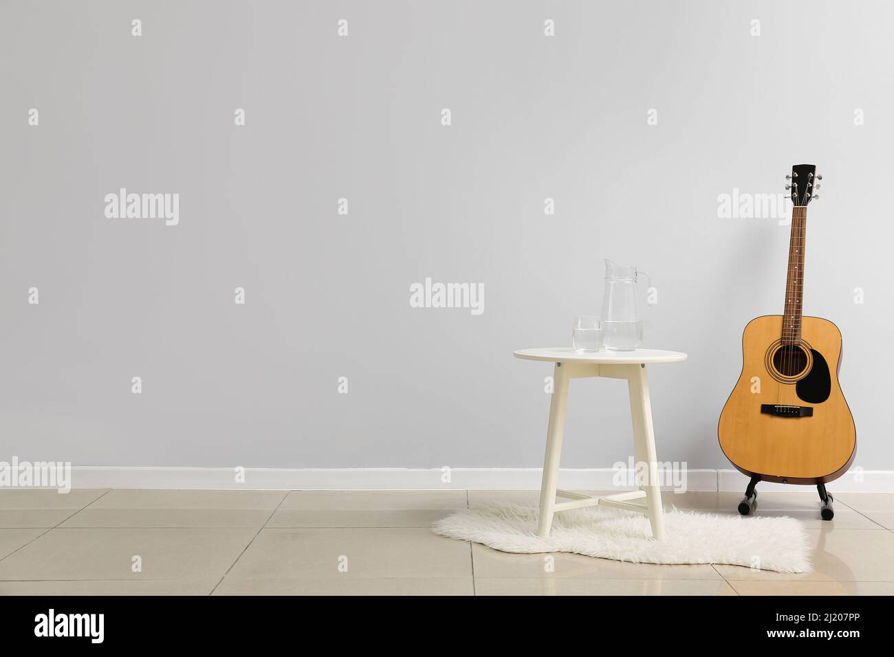 Jug with glass of water on table and guitar near light wall Stock Photo ...