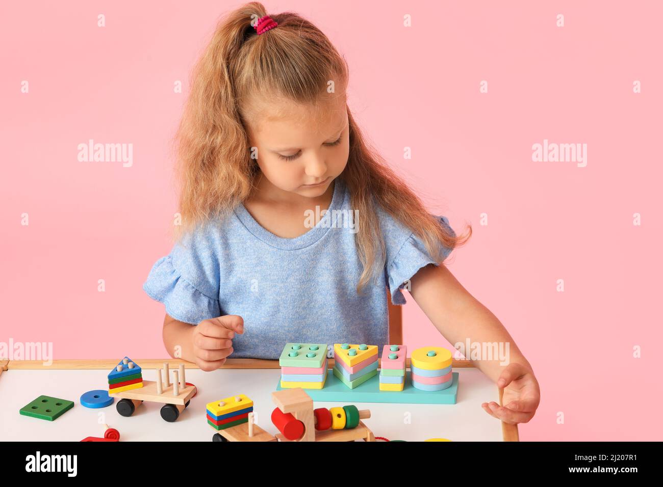 Cute little girl playing with building blocks at table on pink ...