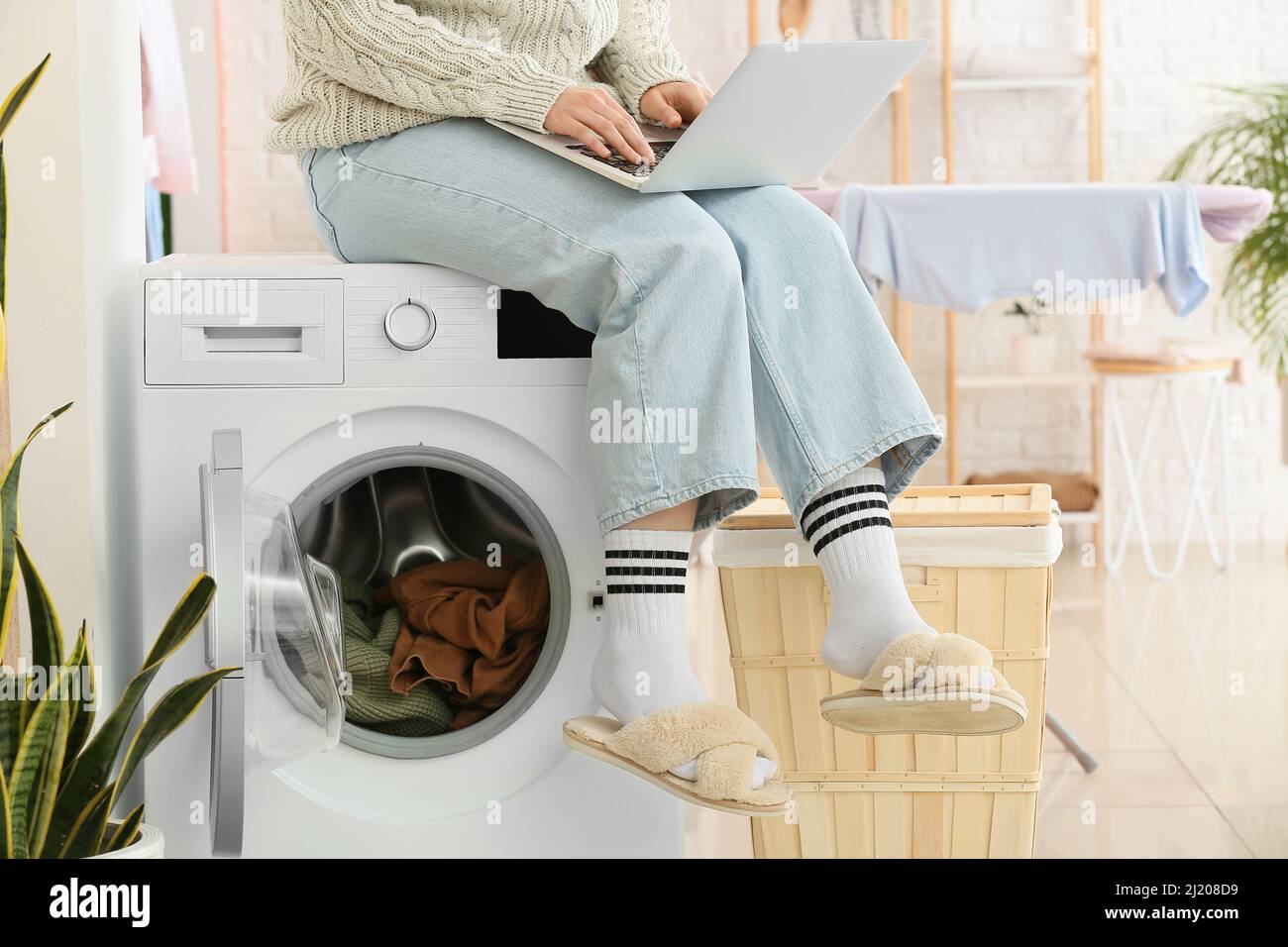 Woman with laptop sitting on washing machine in laundry room Stock Photo - Alamy