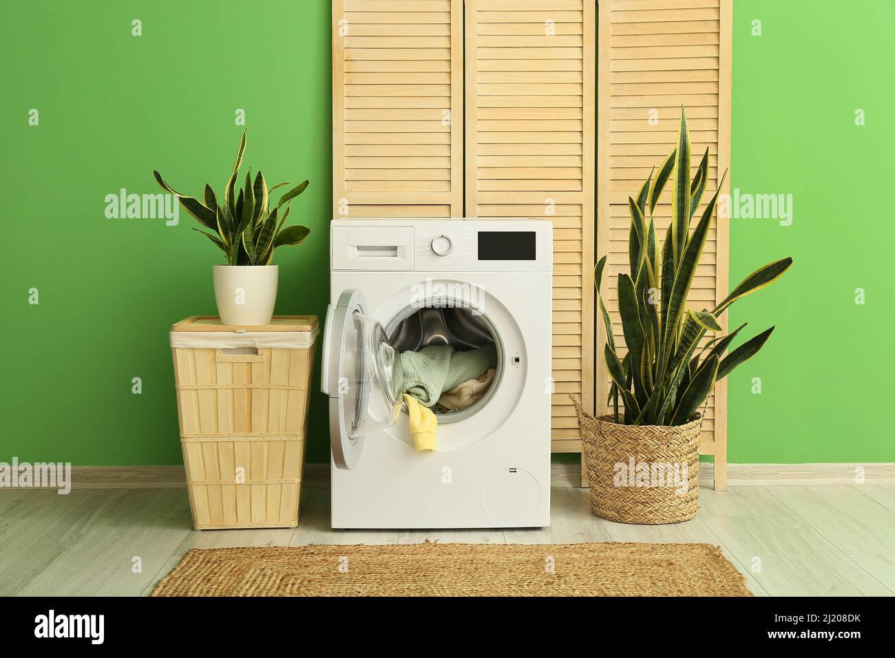 Modern washing machine with laundry, basket and plants near color wall ...