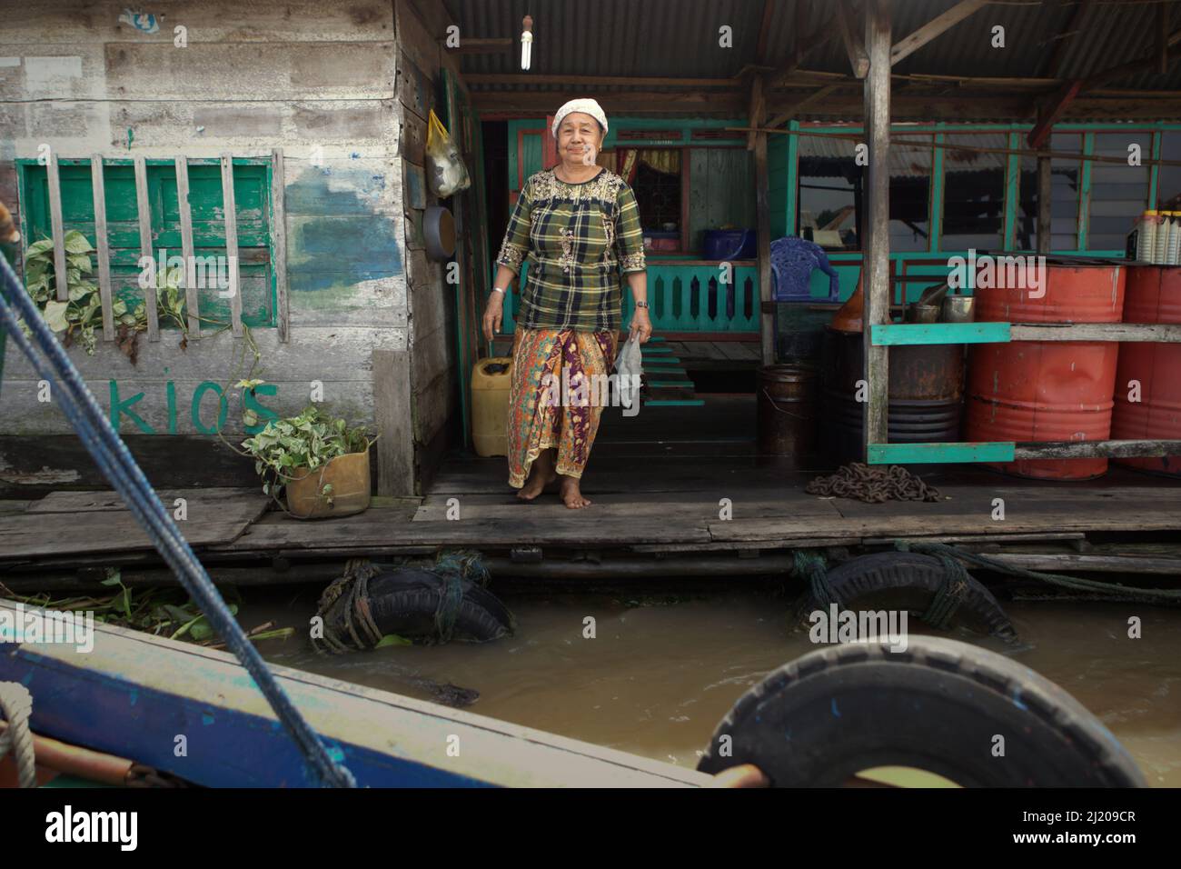 Portrait of a woman standing at the edge of her floating house in ...