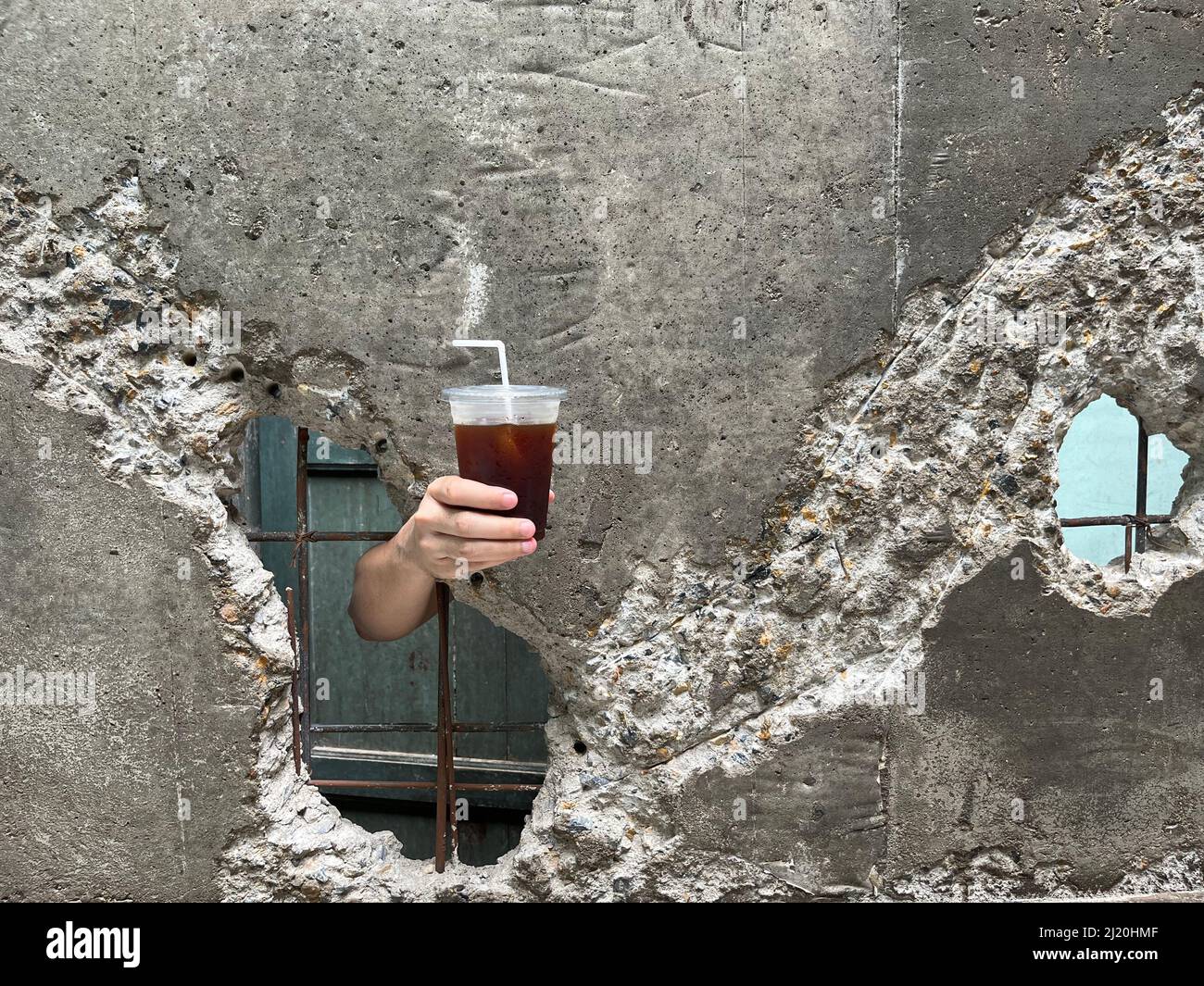 Hand holding iced coffee from the break gap of old wall. Summer drink ...