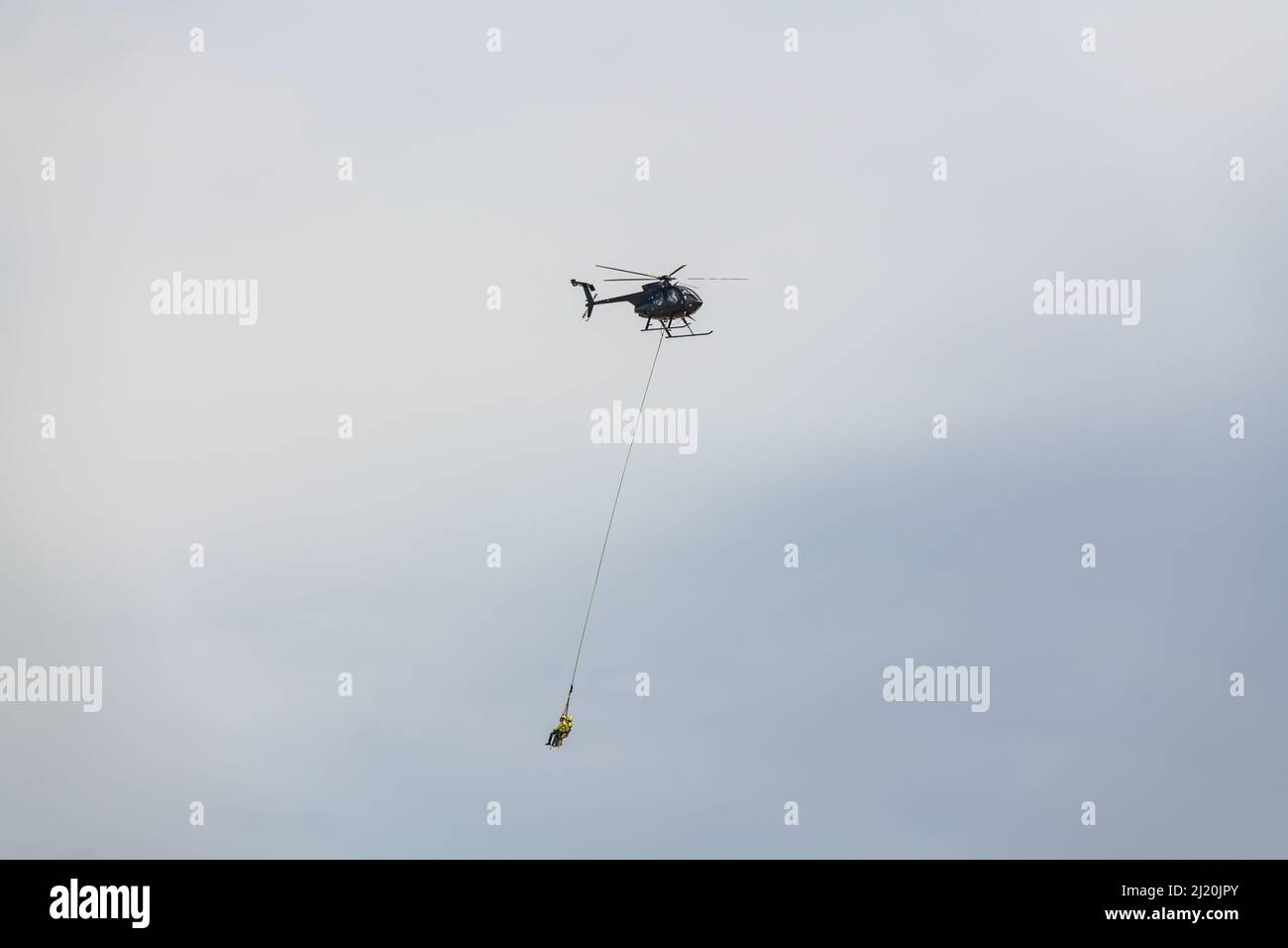 Helicopter seen flying carrying a load below with cloudy, blue sky ...