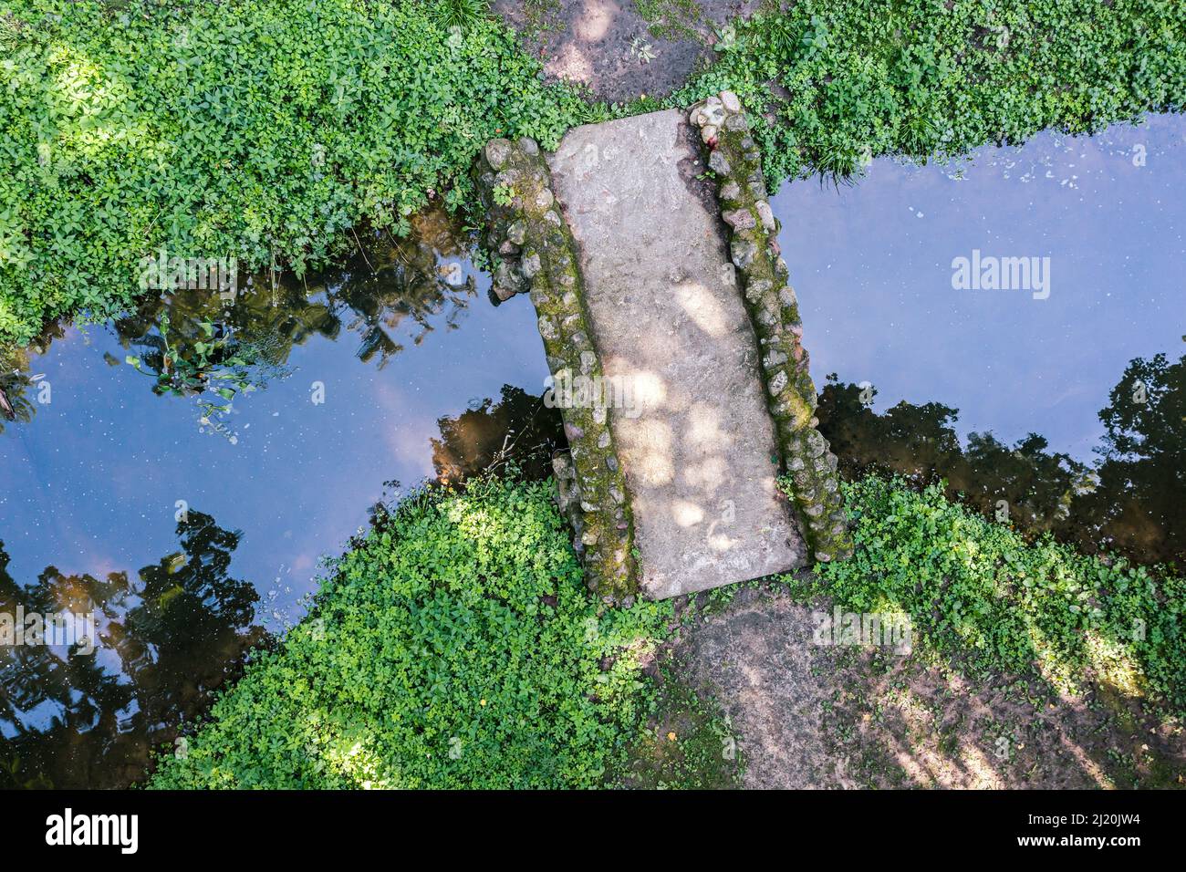 small stone footbridge over calm stream. water with reflections of sky ...