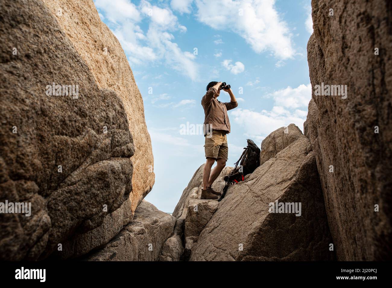 Wilderness explorer looking far away through telescope in rocky valley ...