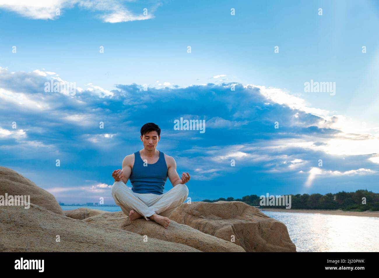 Muscular young man meditating on a beach rock - stock photo Stock Photo ...