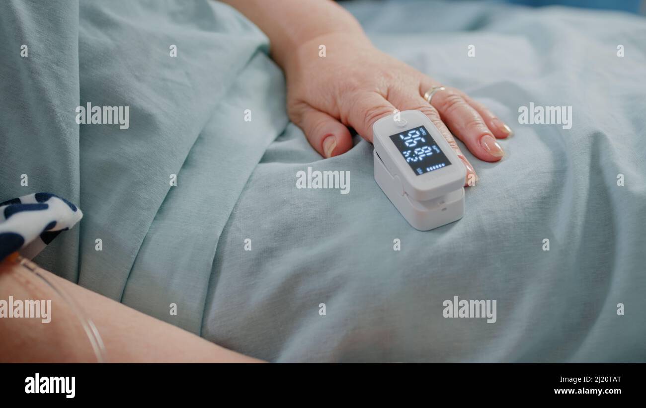 Close up of hand of aged patient with oximeter in bed. Senior person ...