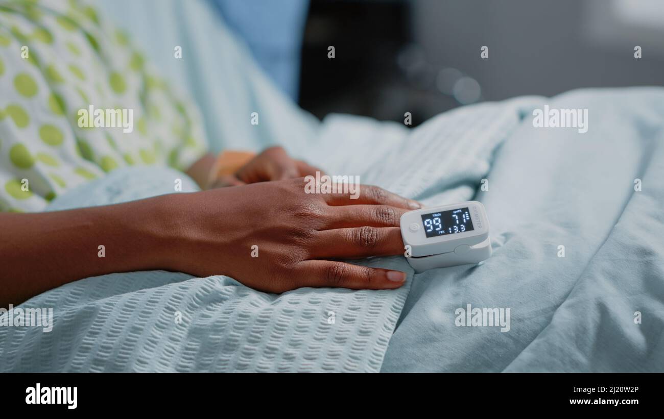 Close up of oximeter on finger of patient with illness in hospital ward ...