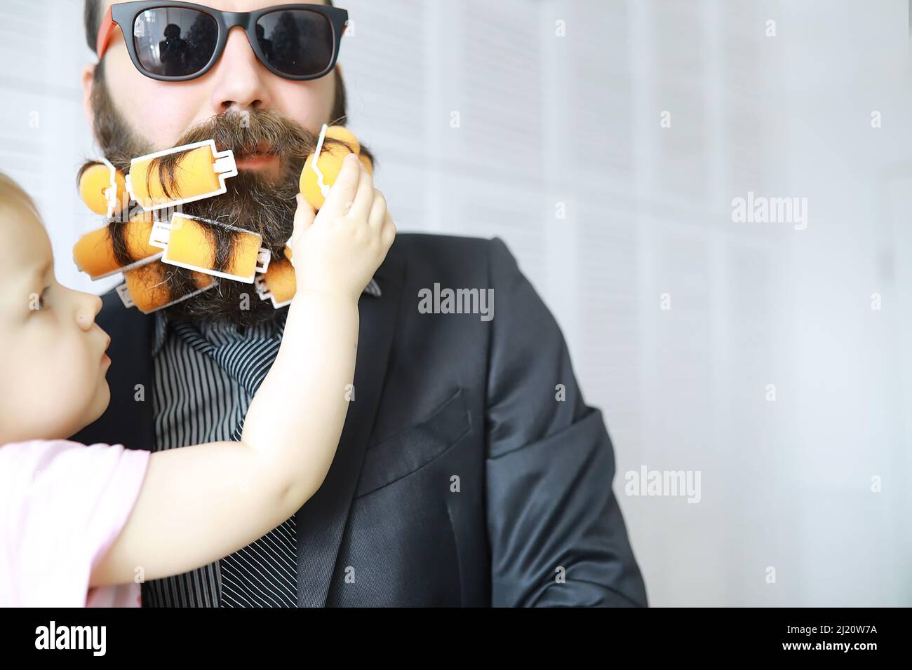 Baby infant hands grab beard of man.Cheerful hipster man curlers in a ...
