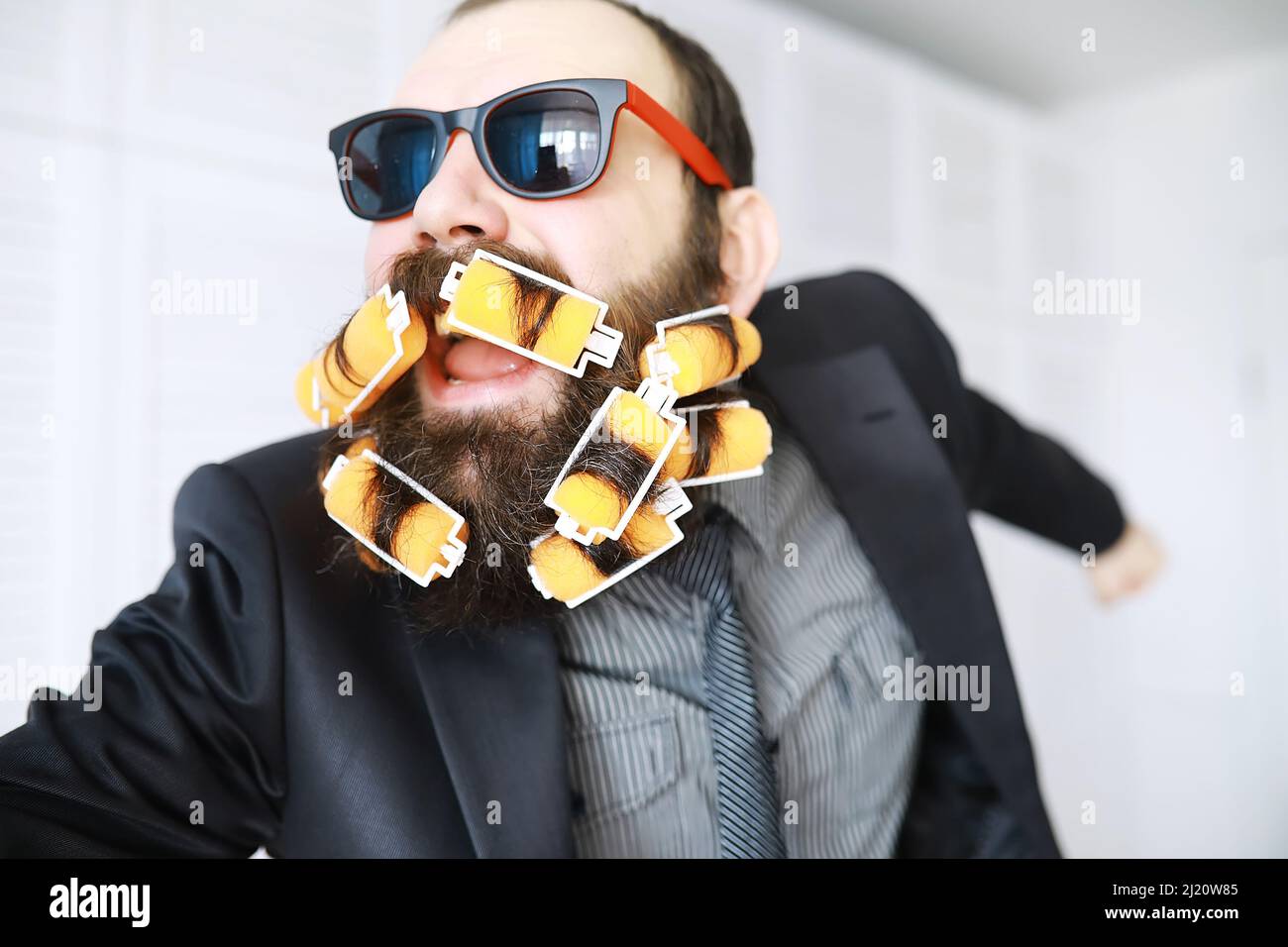 Cheerful hipster man with curlers in beard. Surprised man with glasses ...
