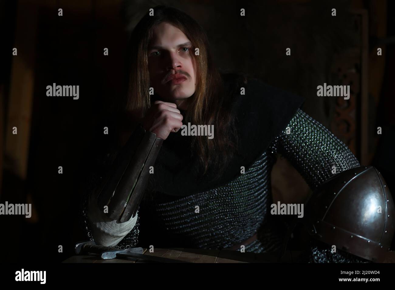 A mighty hero with long hair in chain mail armor in an ancient hall. Medieval warrior in knight ...