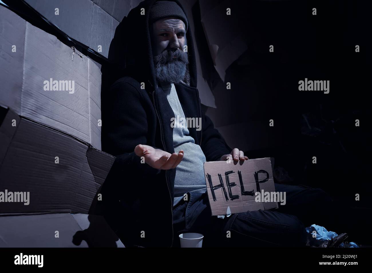 A homeless bearded man sits on boxes on street and asks for help. Need ...