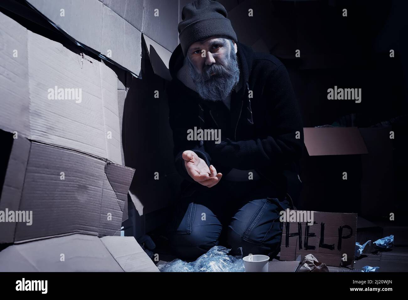 A homeless bearded man sits on boxes on street and asks for help. Need ...
