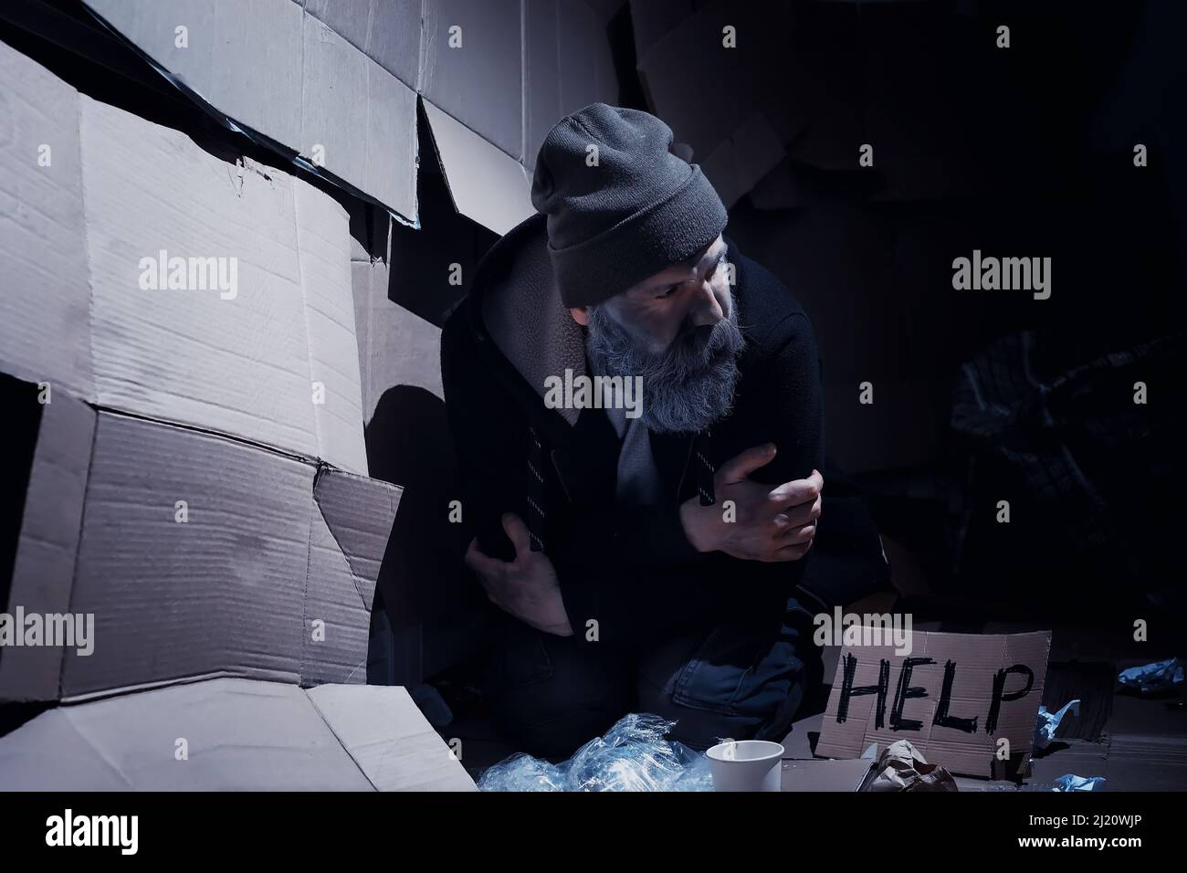 A homeless bearded man sits on boxes on street and asks for help. Need ...