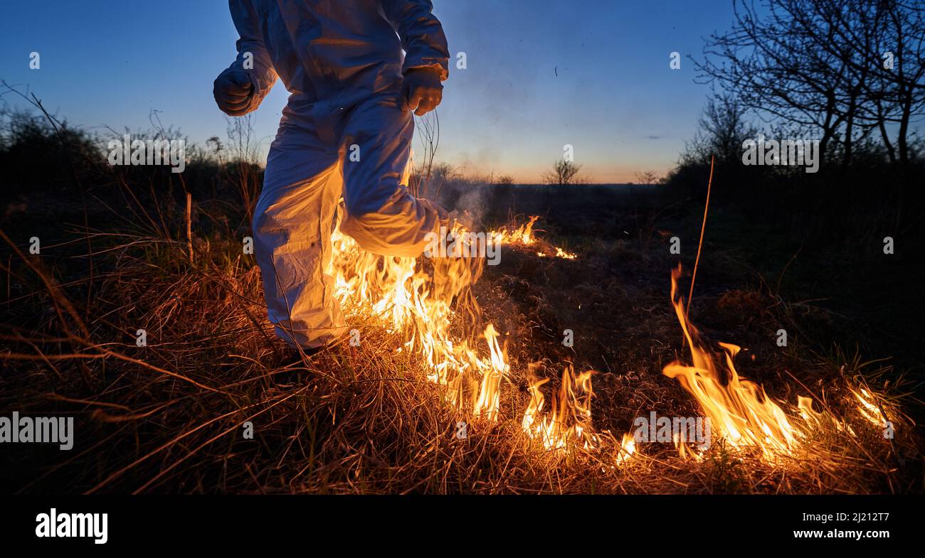 Firefighter ecologist extinguishing fire in field at night. Cropped ...
