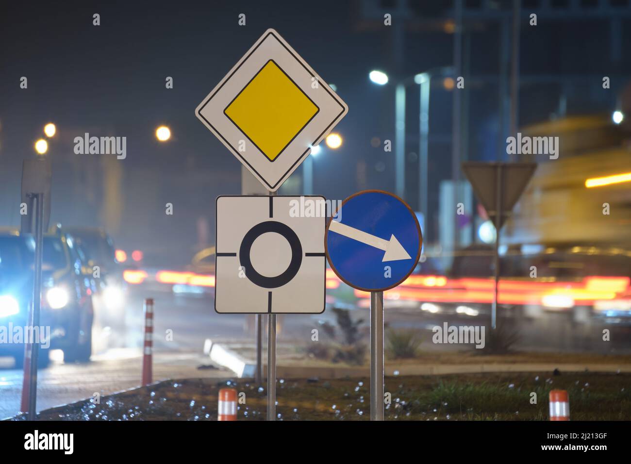 Roundabout road signs with blurred cars on city street traffic at night ...
