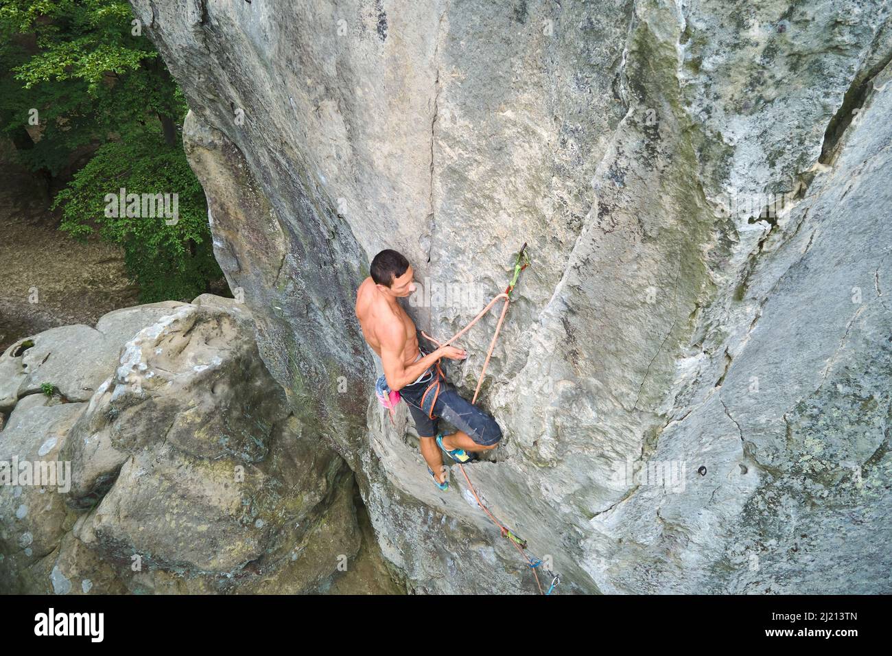 Young man climbing steep wall of rocky mountain. Male climber overcomes ...