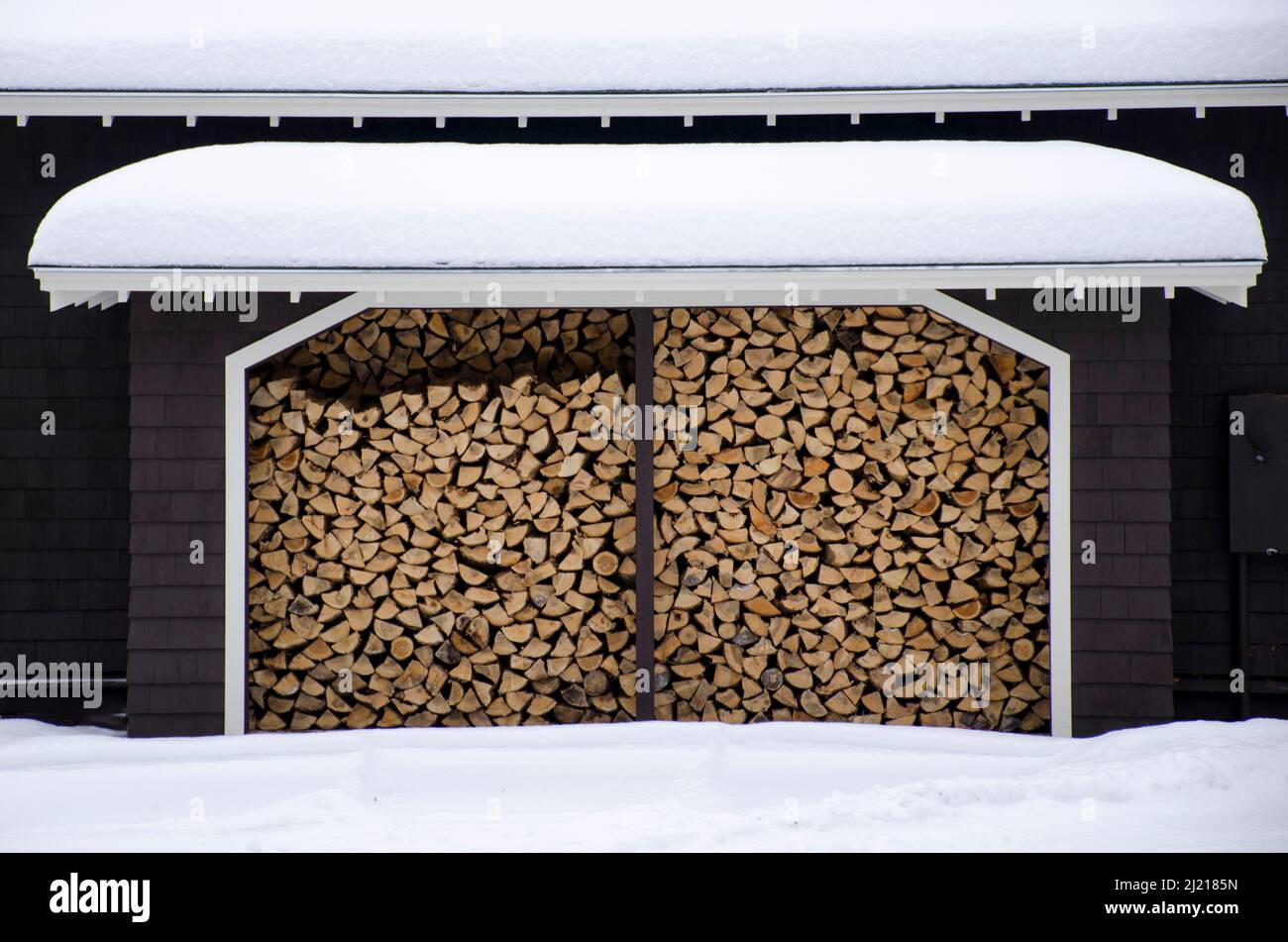 Pile of firewood stacked inside a shed. Snow covered garage filled with ...