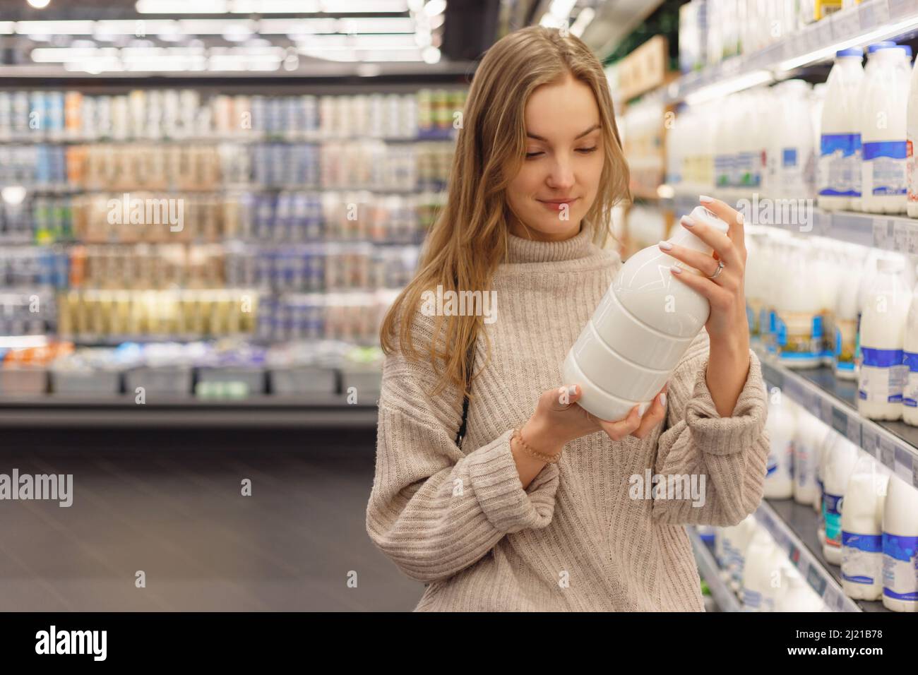 Grocery Shopping. Female read milk bottle In shop standing near shelf ...
