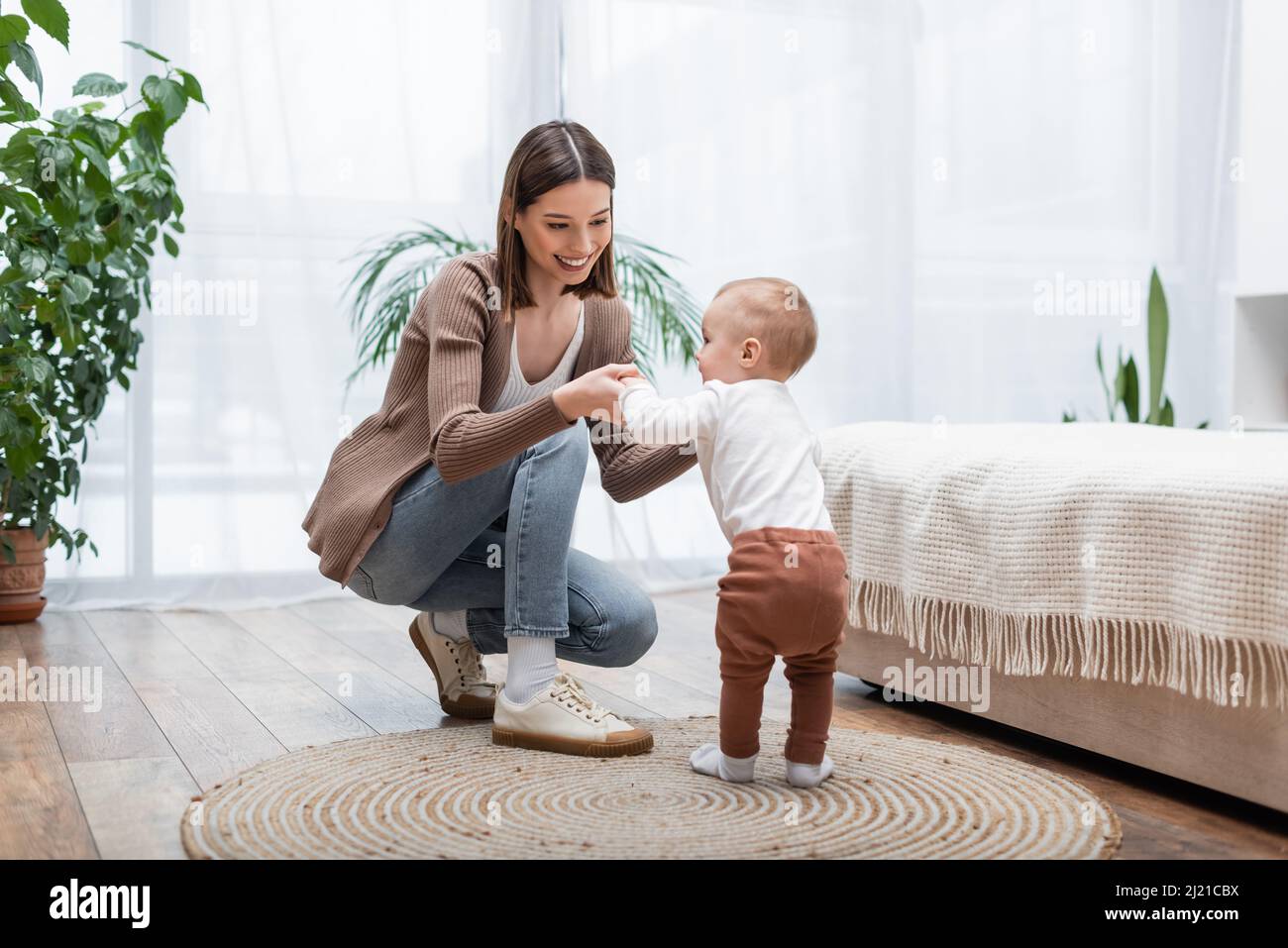 Young parent holding hand of infant boy on rug in bedroom Stock Photo ...