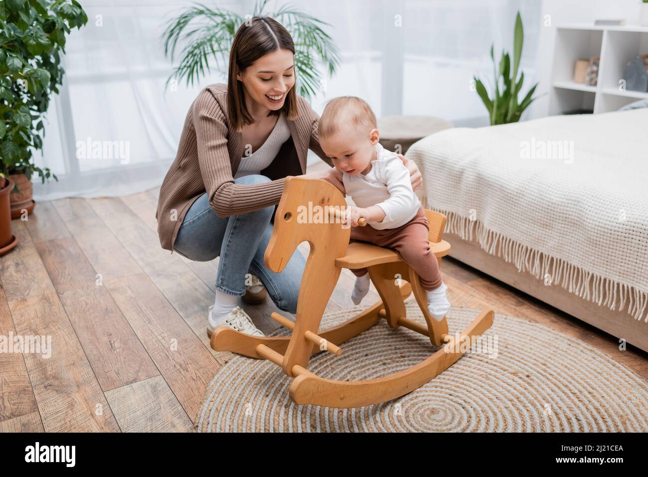 Young woman holding baby on rocking horse at home Stock Photo - Alamy