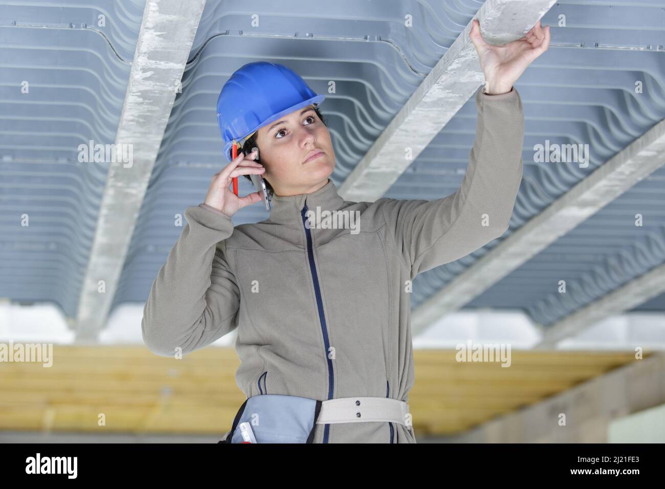 female contractor examining concrete roof support and using smartphone ...